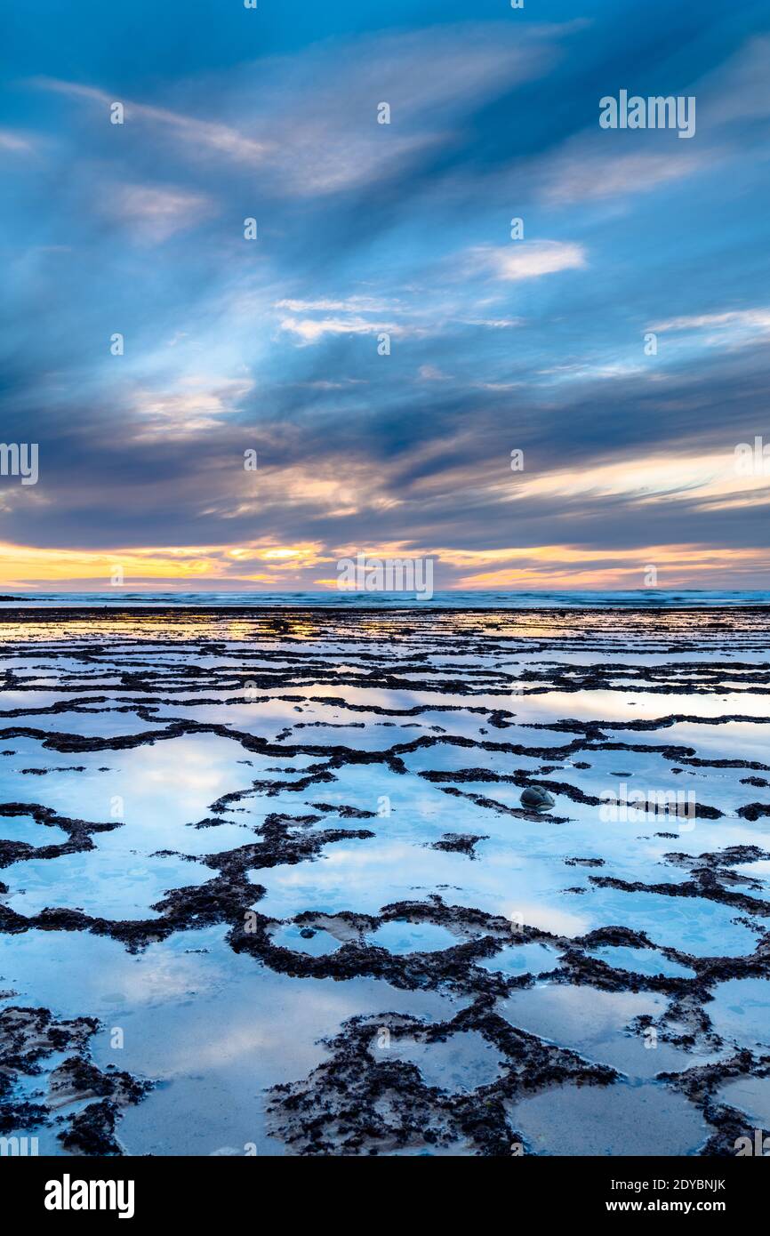 A vertical view of a beautiful sunset over the ocean with rocky beach ...