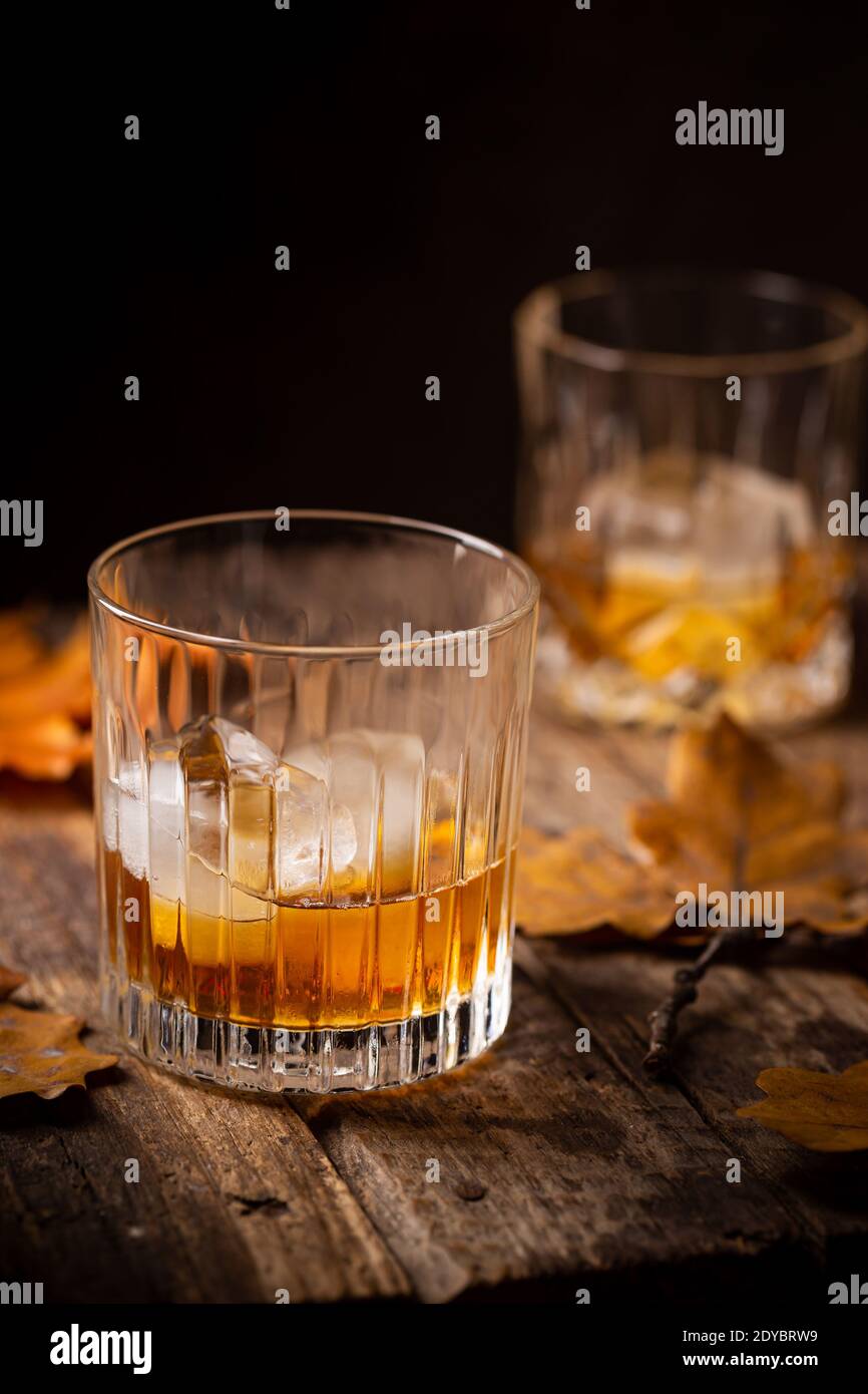 Glass of scotch whiskey and ice on wooden background with autumn leaves ...