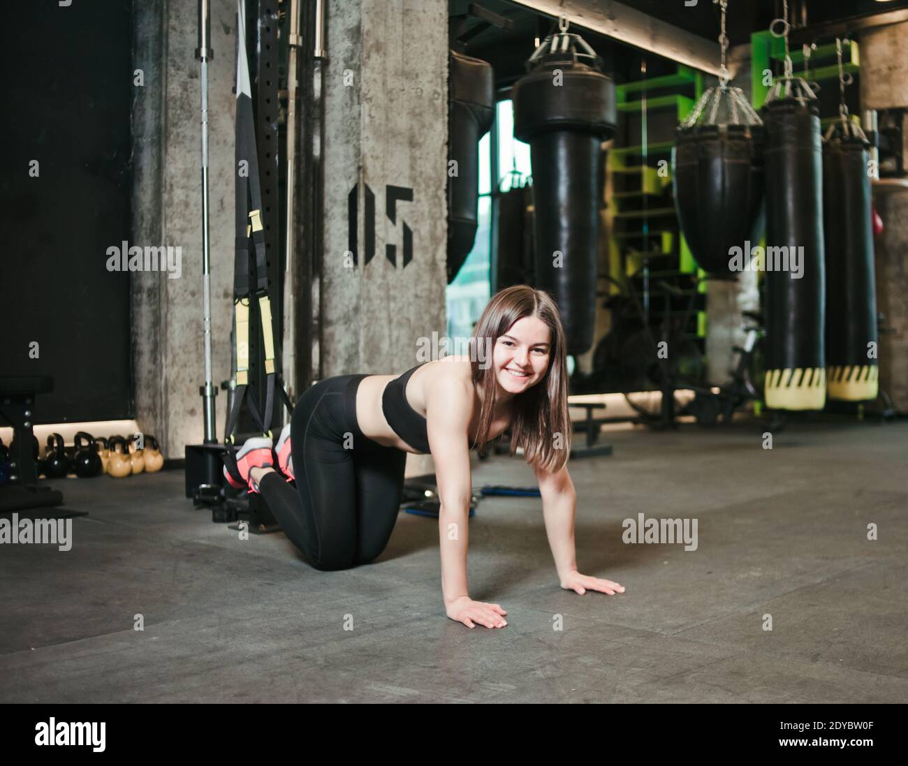 Young woman doing push-ups while legs hanging on trx at gym. Functional ...