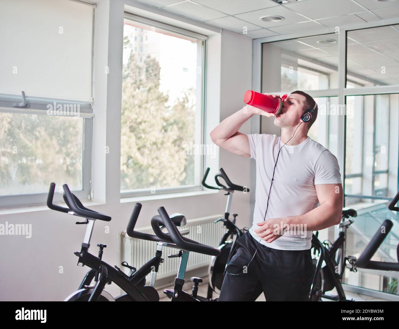 Man drinking water and listening music on exercise bike at spinning ...