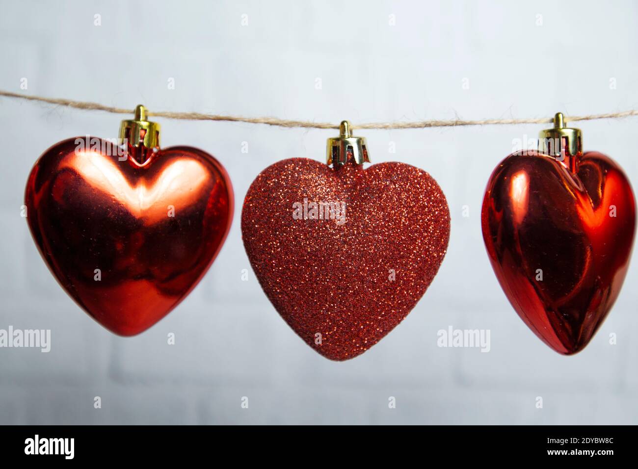 red hearts hang on a thread on a white brick background Stock Photo - Alamy