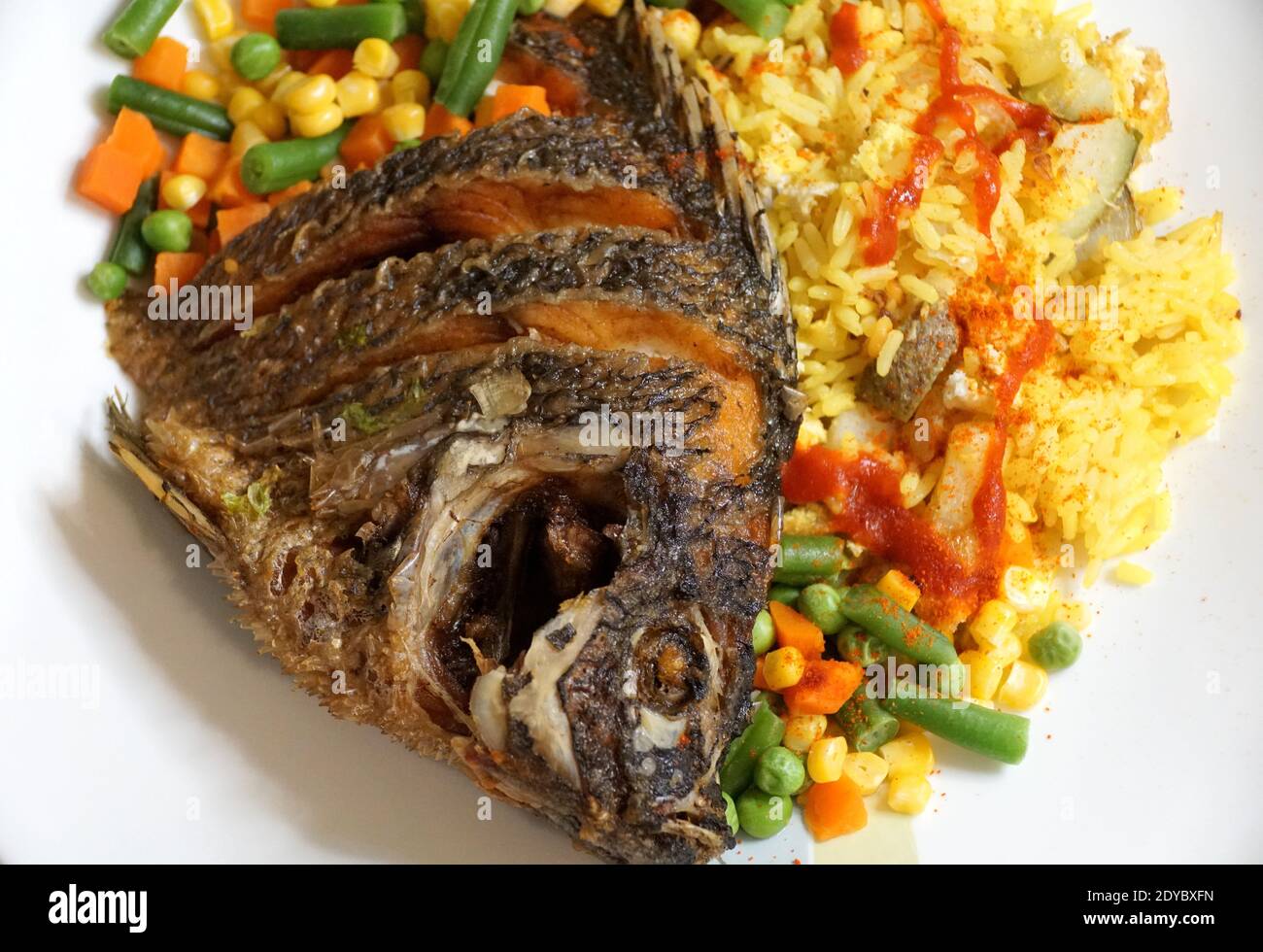 Fried tilapia with yellow rice and mixed vegetable on a white plate ...