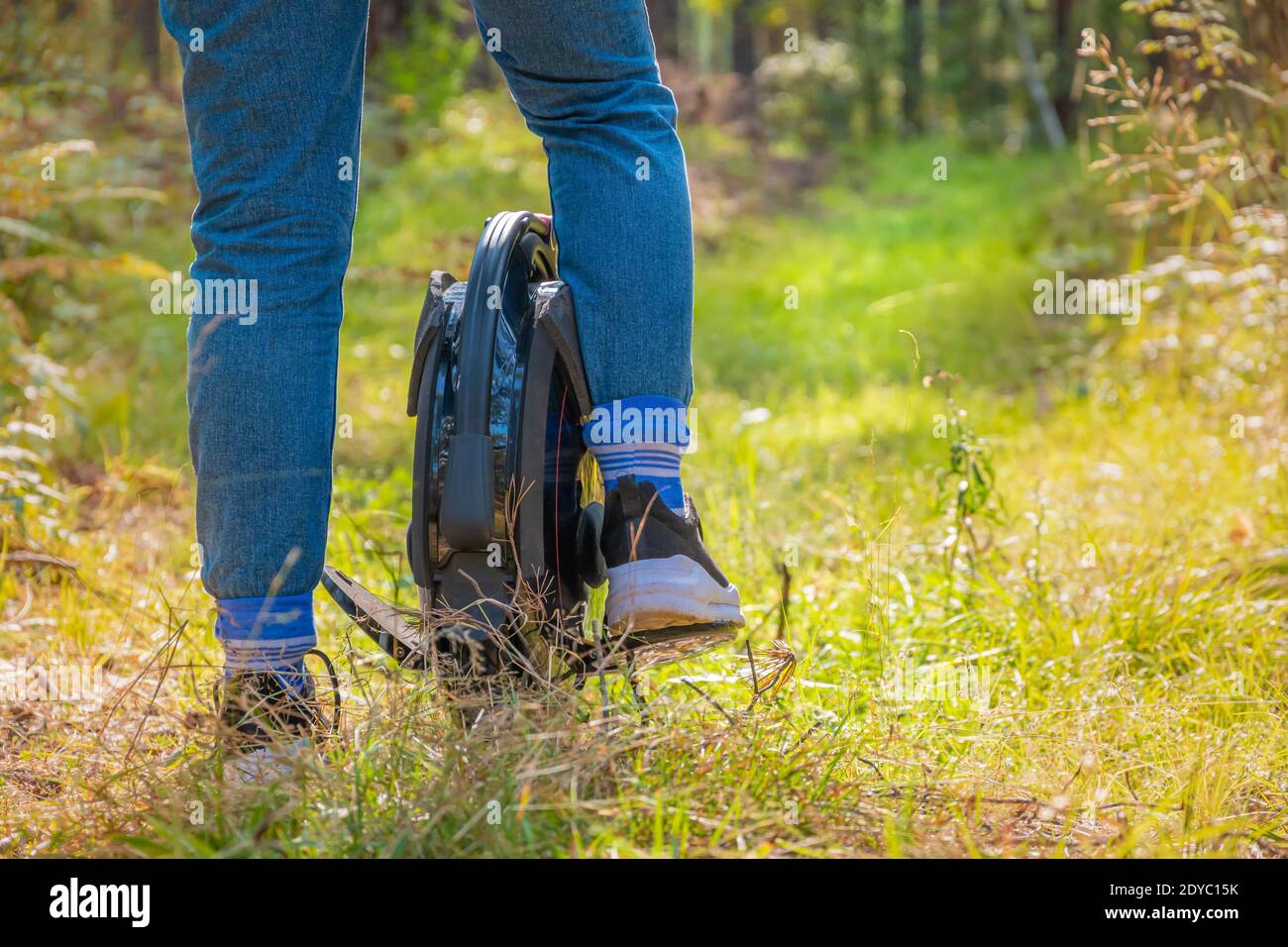 Rear view of women's legs on an electric unicycle in the forest on a ...