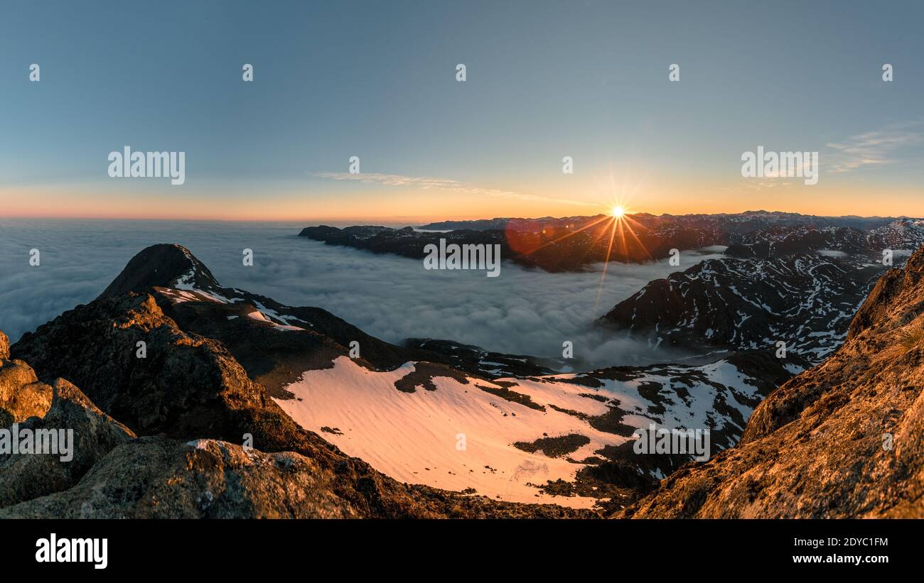 An aerial shot of the snowy mountains peaks above the clouds during the sunrise Stock Photo - Alamy