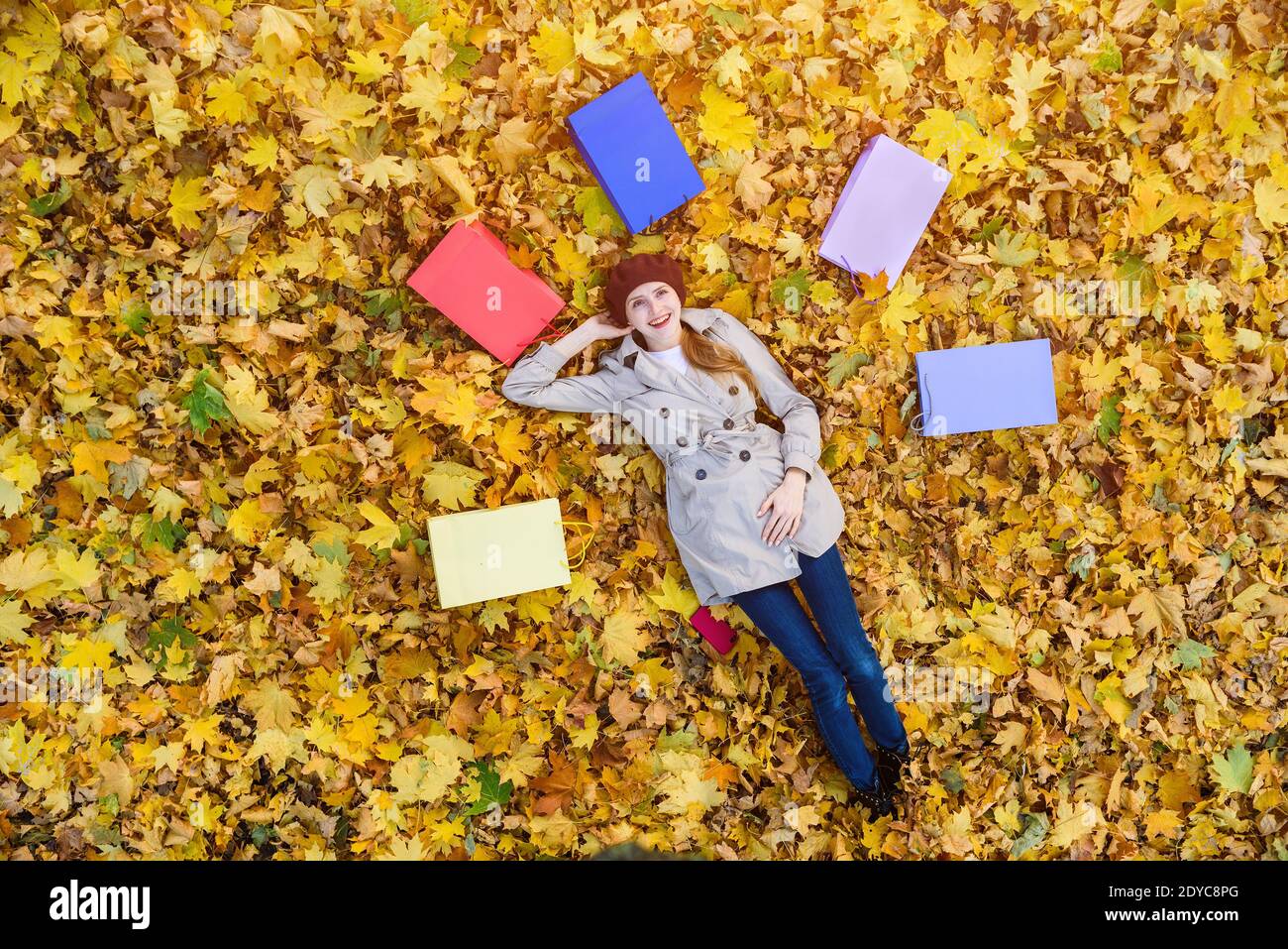 Happy woman after shopping. Girl lying on autumn leaves near colorful ...