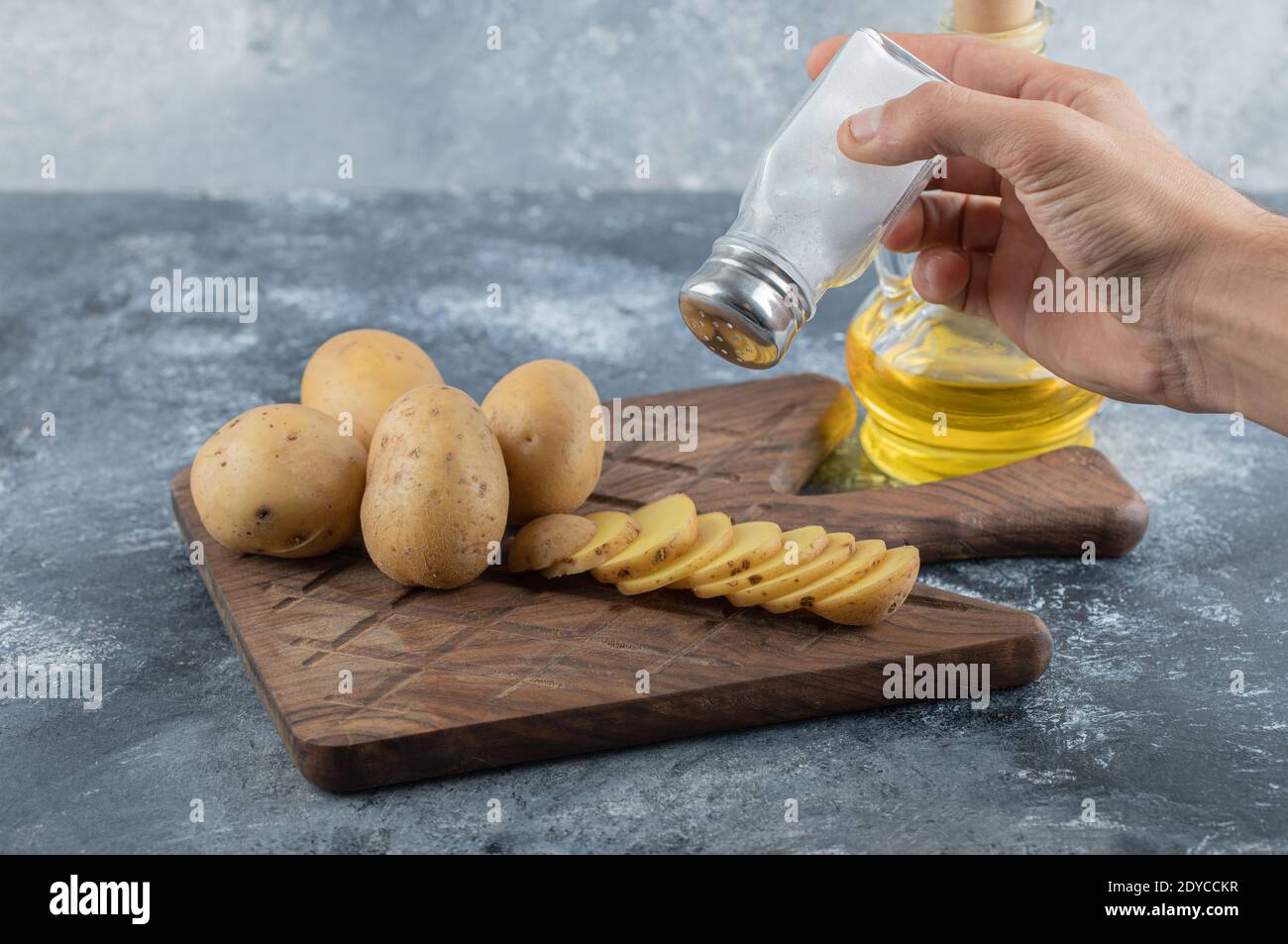 Man pouring salt over the sliced potatoes Stock Photo - Alamy