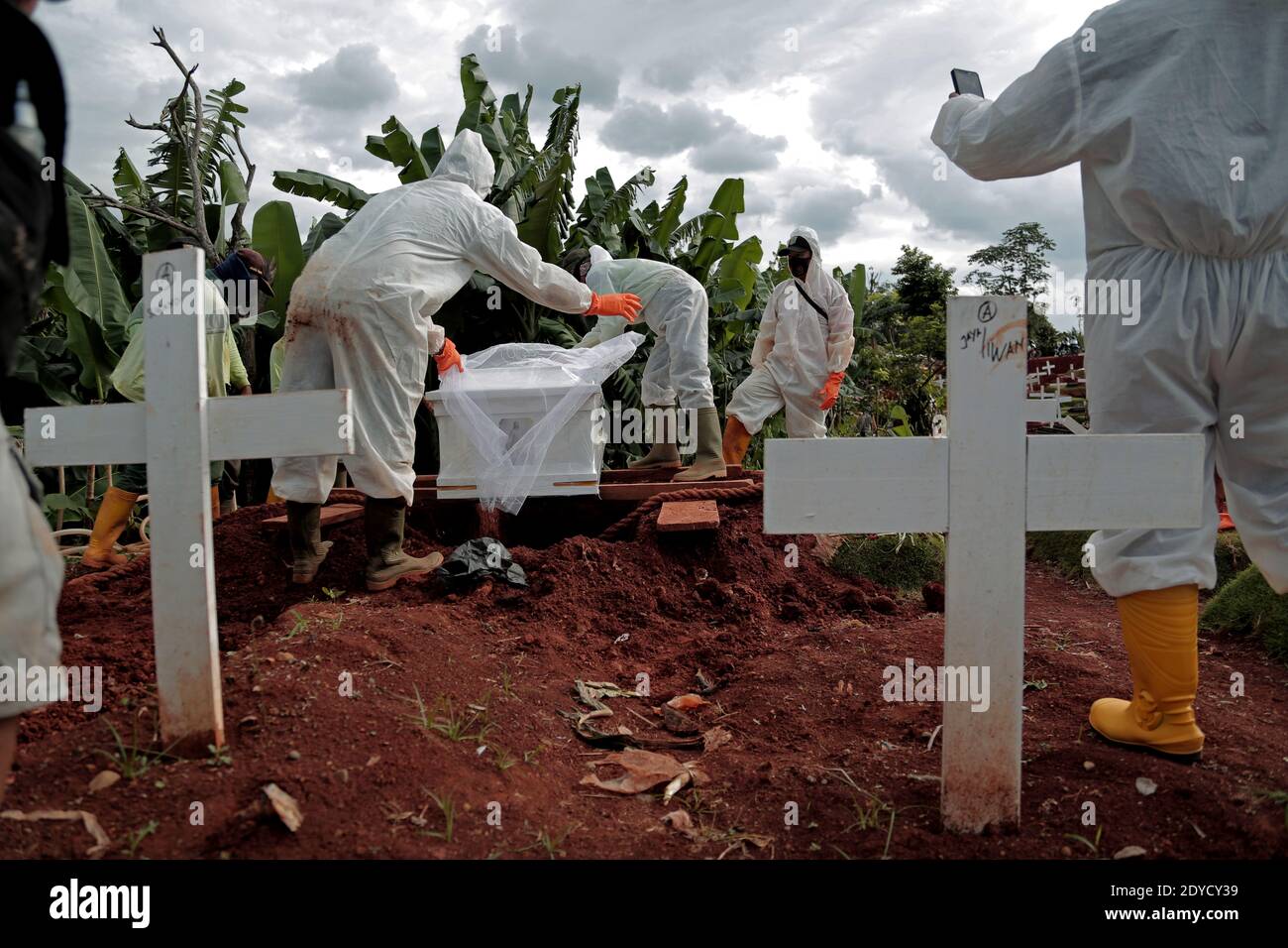 Funeral workers wearing personal protective equipment (PPE) burying a ...