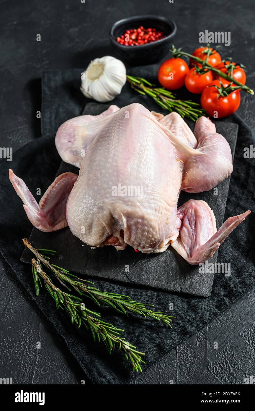 Raw whole chicken with rosemary and pink pepper. Black background. Top ...