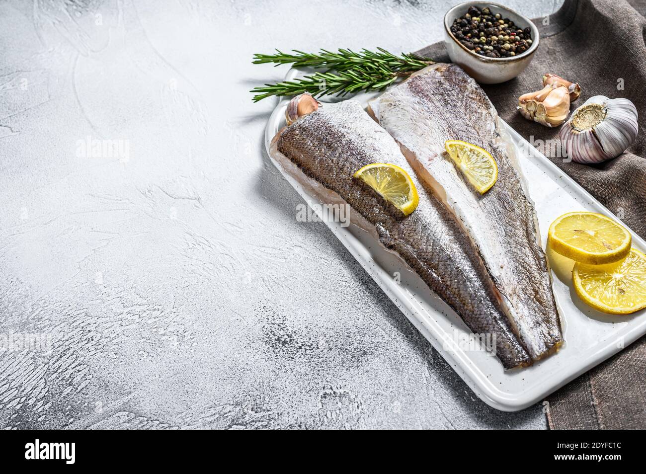 Fresh raw hake fish fillet with pepper and lemon. White background. Top ...