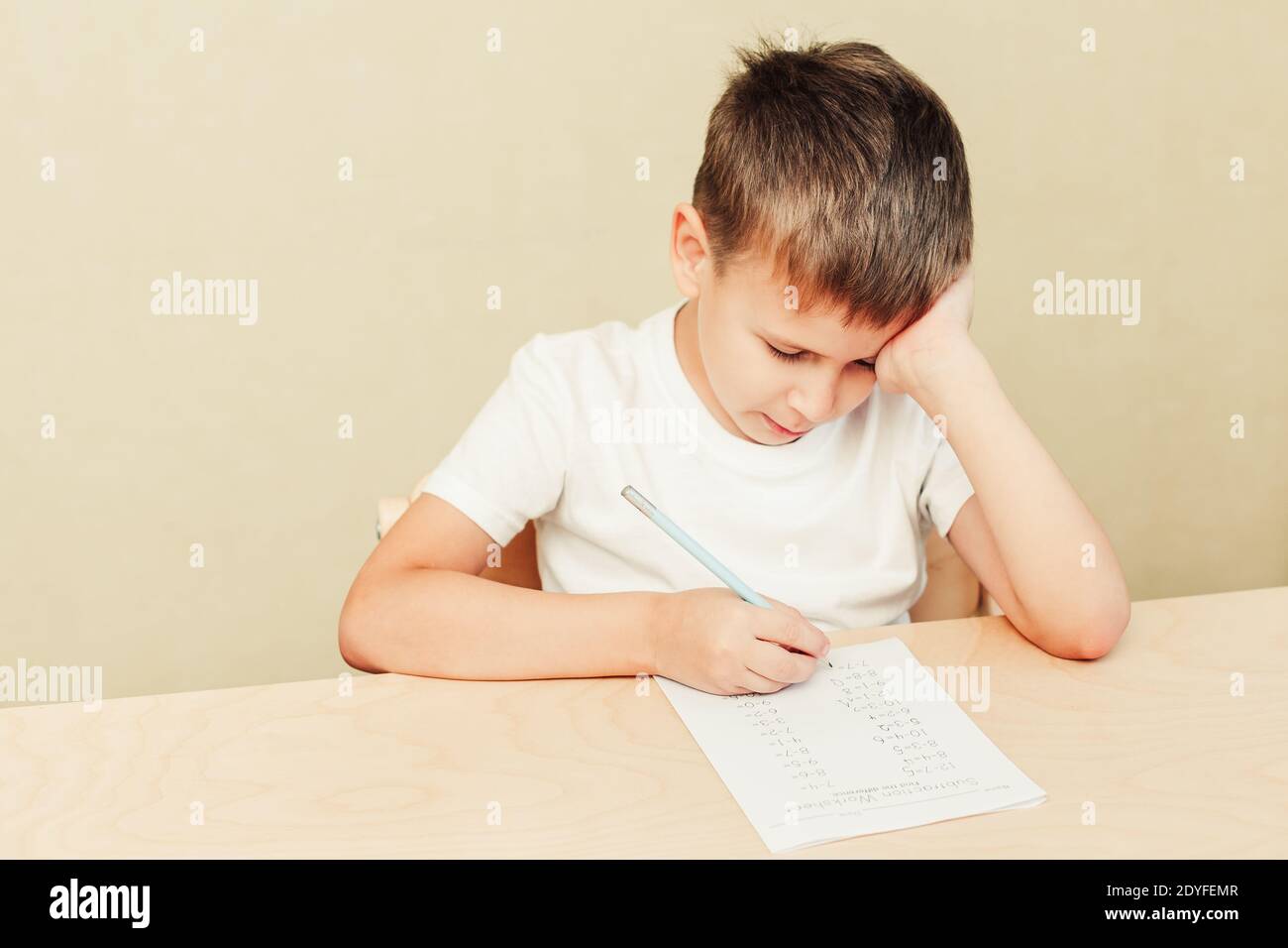 7 years old child boy sitting at desk and writing in sheet of paper ...