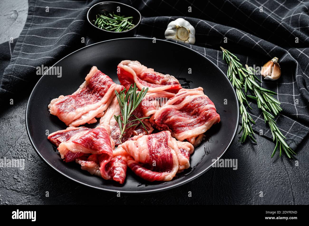 Raw beef bacon, marbled meat in a plate. Black background. Top view ...