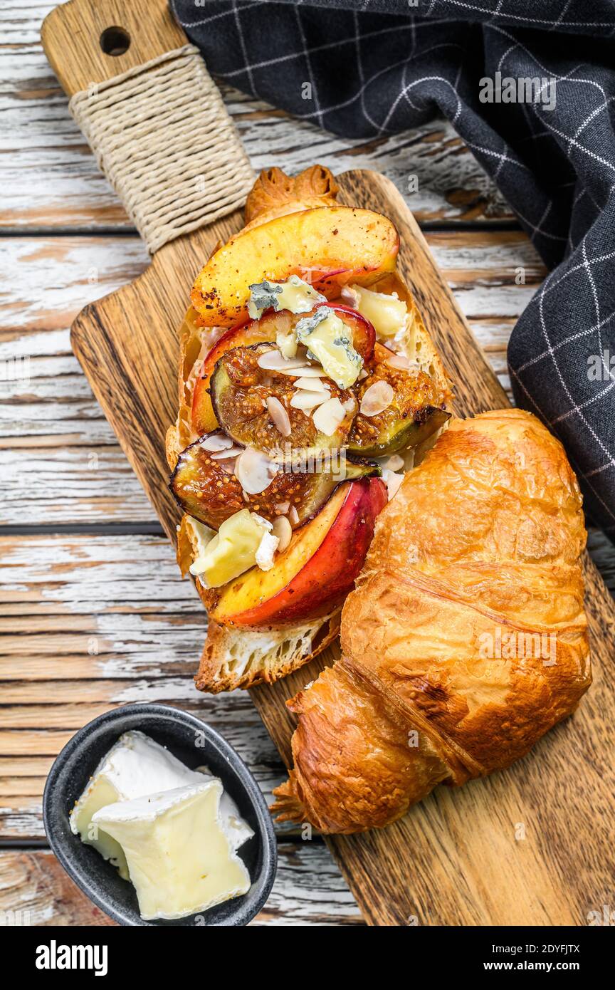 French croissant with bree cheese, peach and figs. White wooden ...