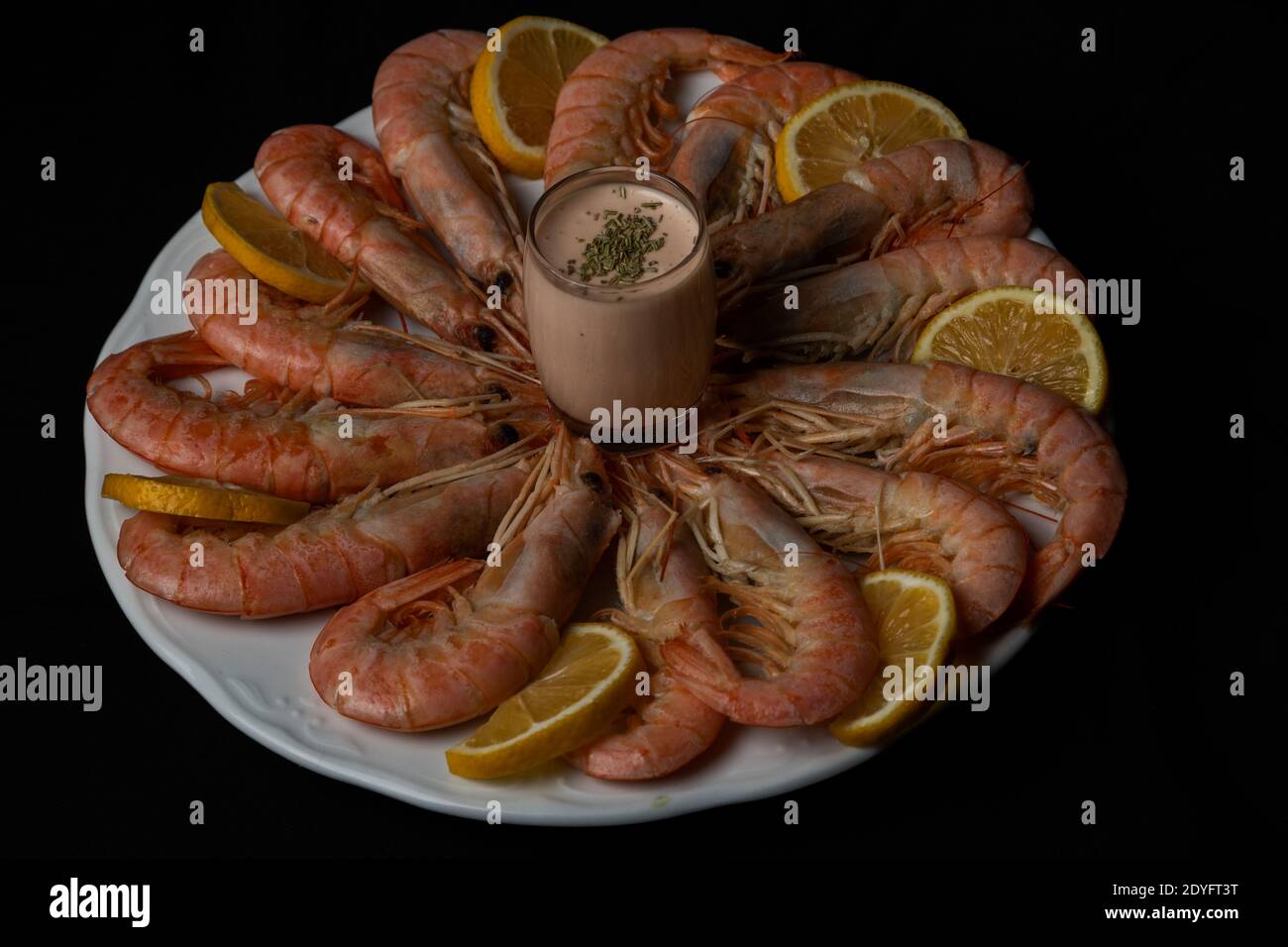 Flat lay image of unpeeled king prawns served with lemon slices and cocktail sauce as a starter ...