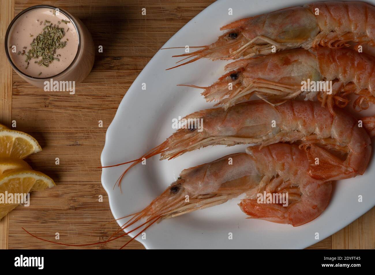 Flat lay image of unpeeled king prawns served with lemon slices and cocktail sauce as a starter ...