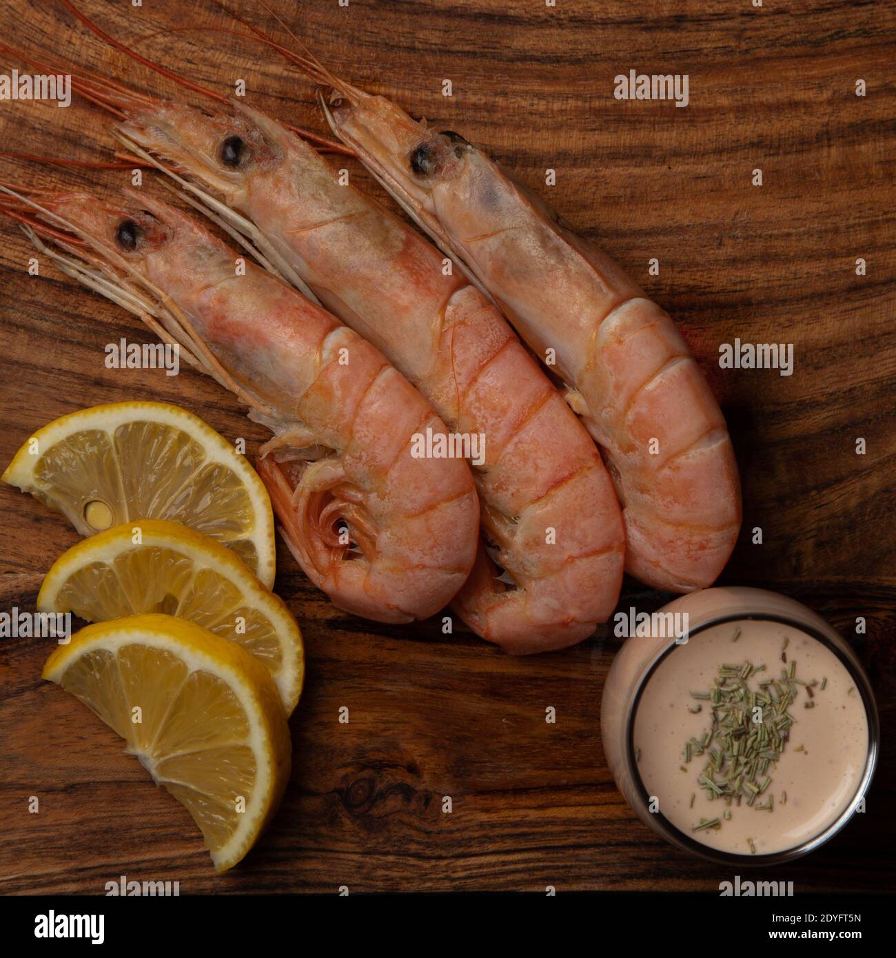 Flat lay image of unpeeled king prawns served with lemon slices and cocktail sauce as a starter ...