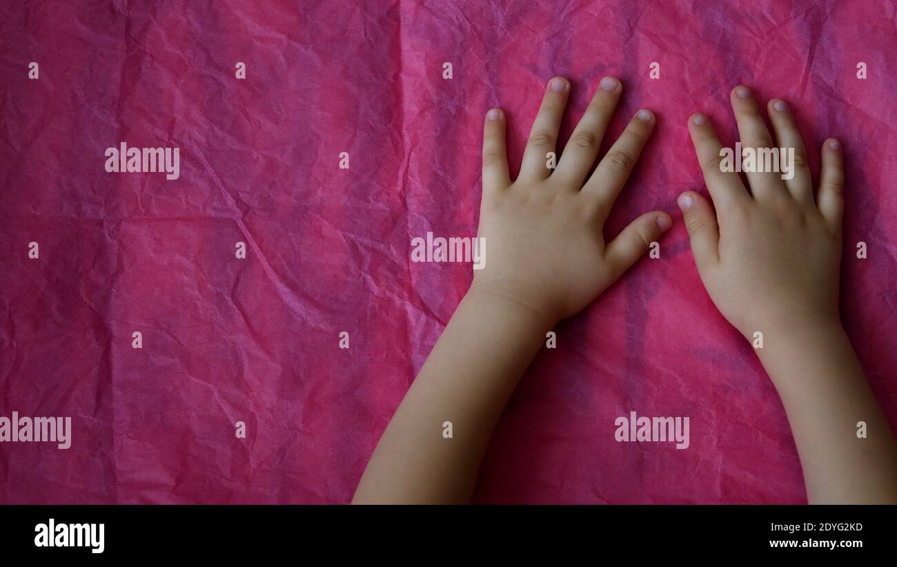 Closeup toddler hands on crumpled pink paper with copy space. Top view ...
