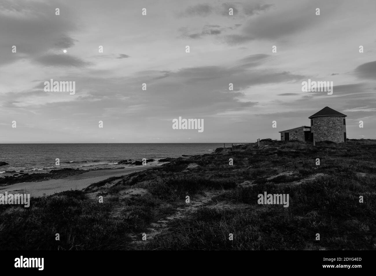 A greyscale shot of a building on the beach by the ocean on a cloudy ...