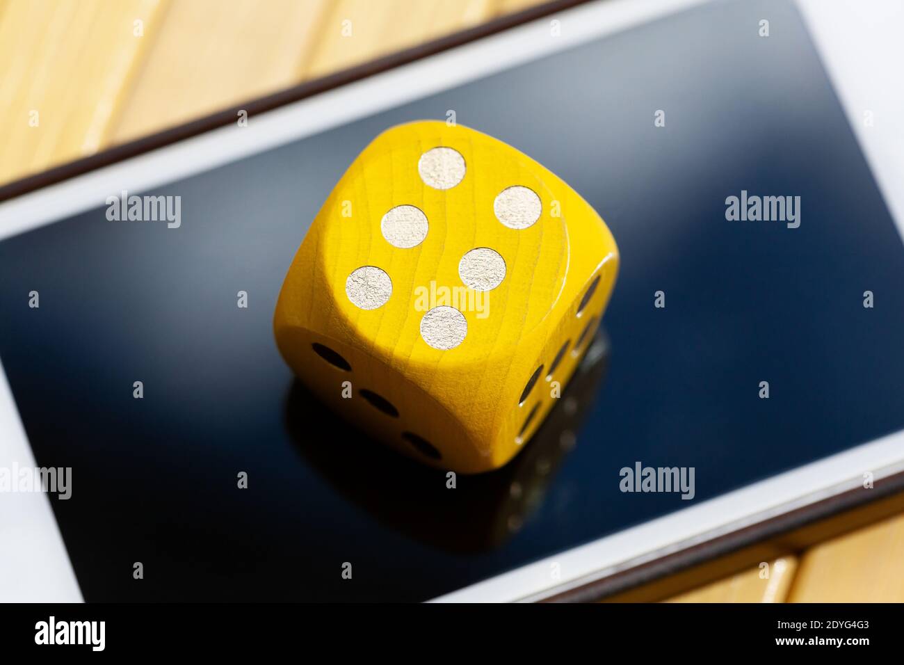 Simple yellow game dice showing six laying on a modern smartphone ...