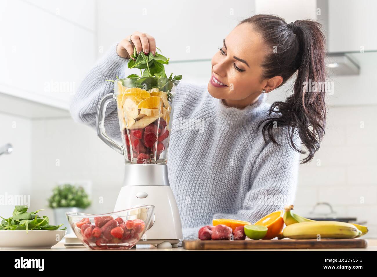 Good looking girl piles colorful mix of fruit and green leaves into a ...