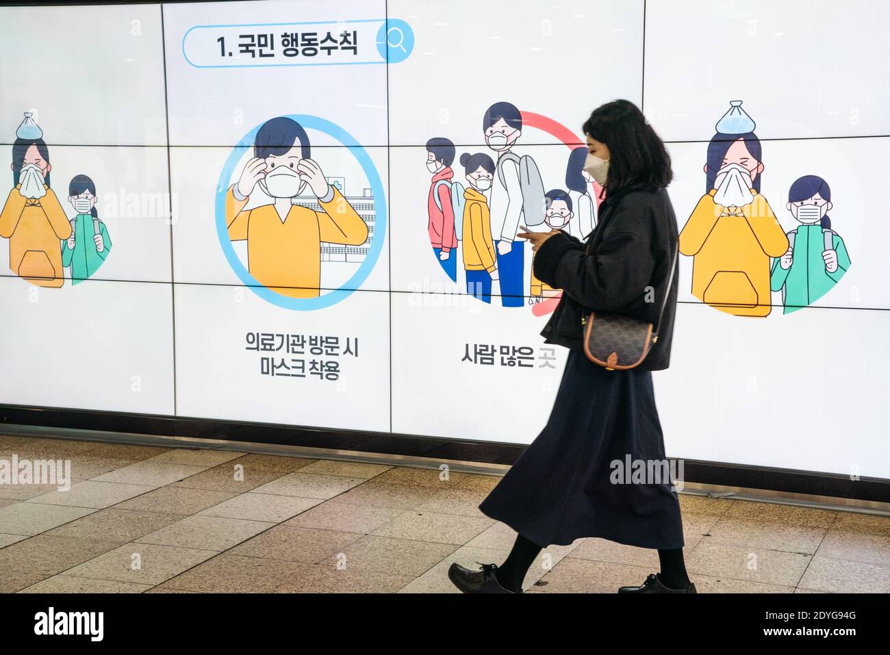 A woman wearing a mask walks past a displayed 'Citizen Behavior ...