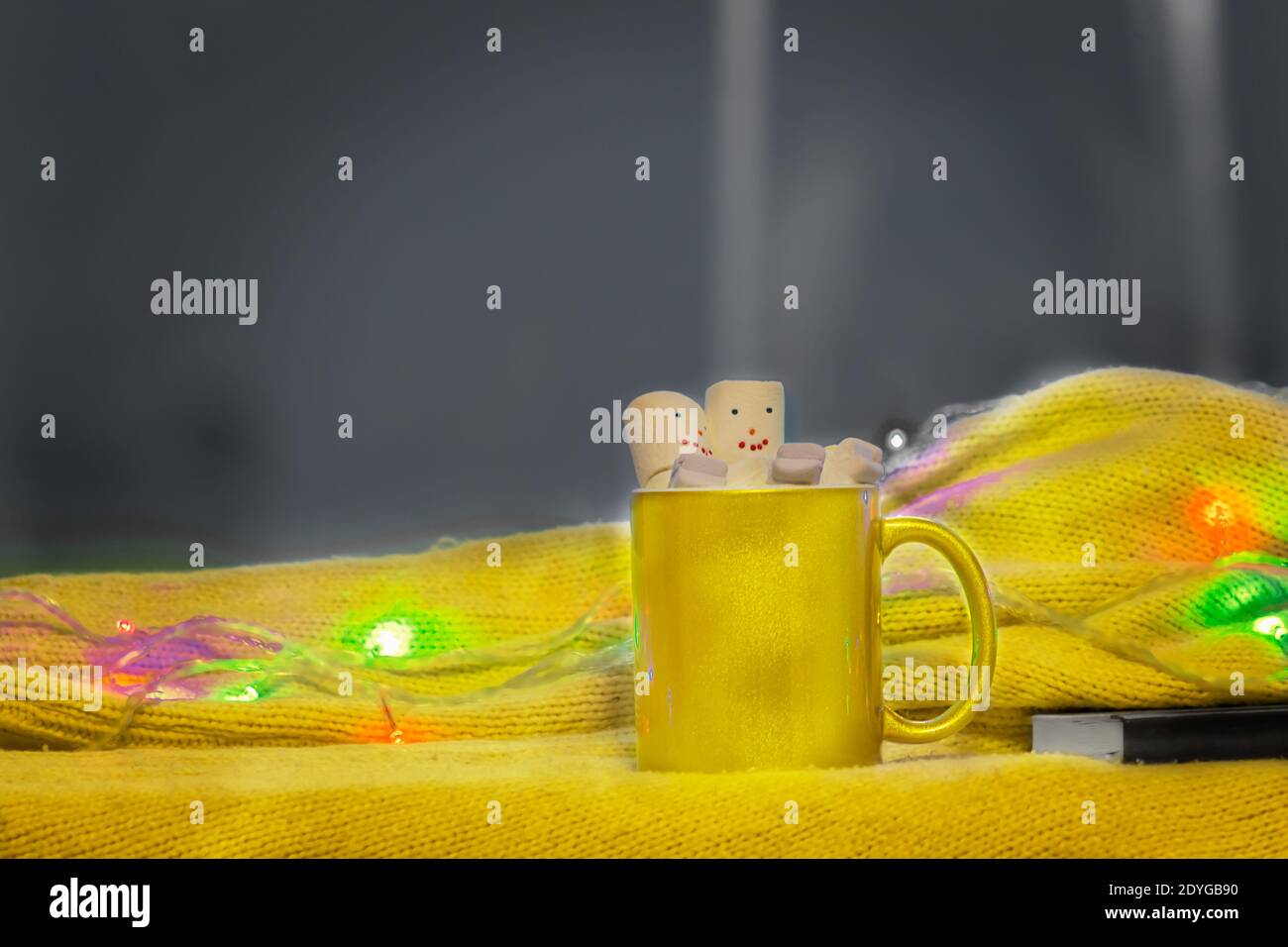 Yellow cup of hot beverage with melted funny marshmallow snowman. Grey ...