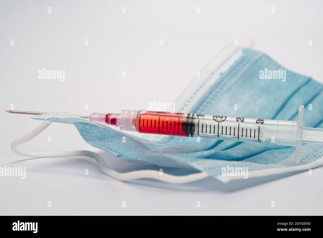 A syringe filled with red liquid, like blood, on a surgical mask ...