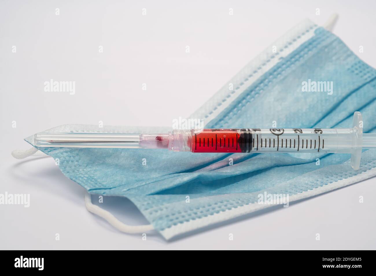 A syringe filled with red liquid, like blood, on a surgical mask ...