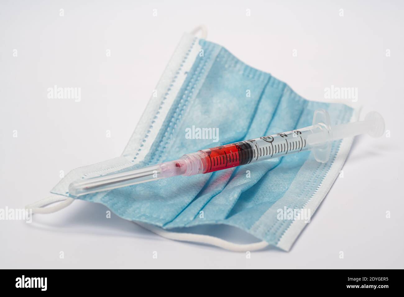 A syringe filled with red liquid, like blood, on a surgical mask ...
