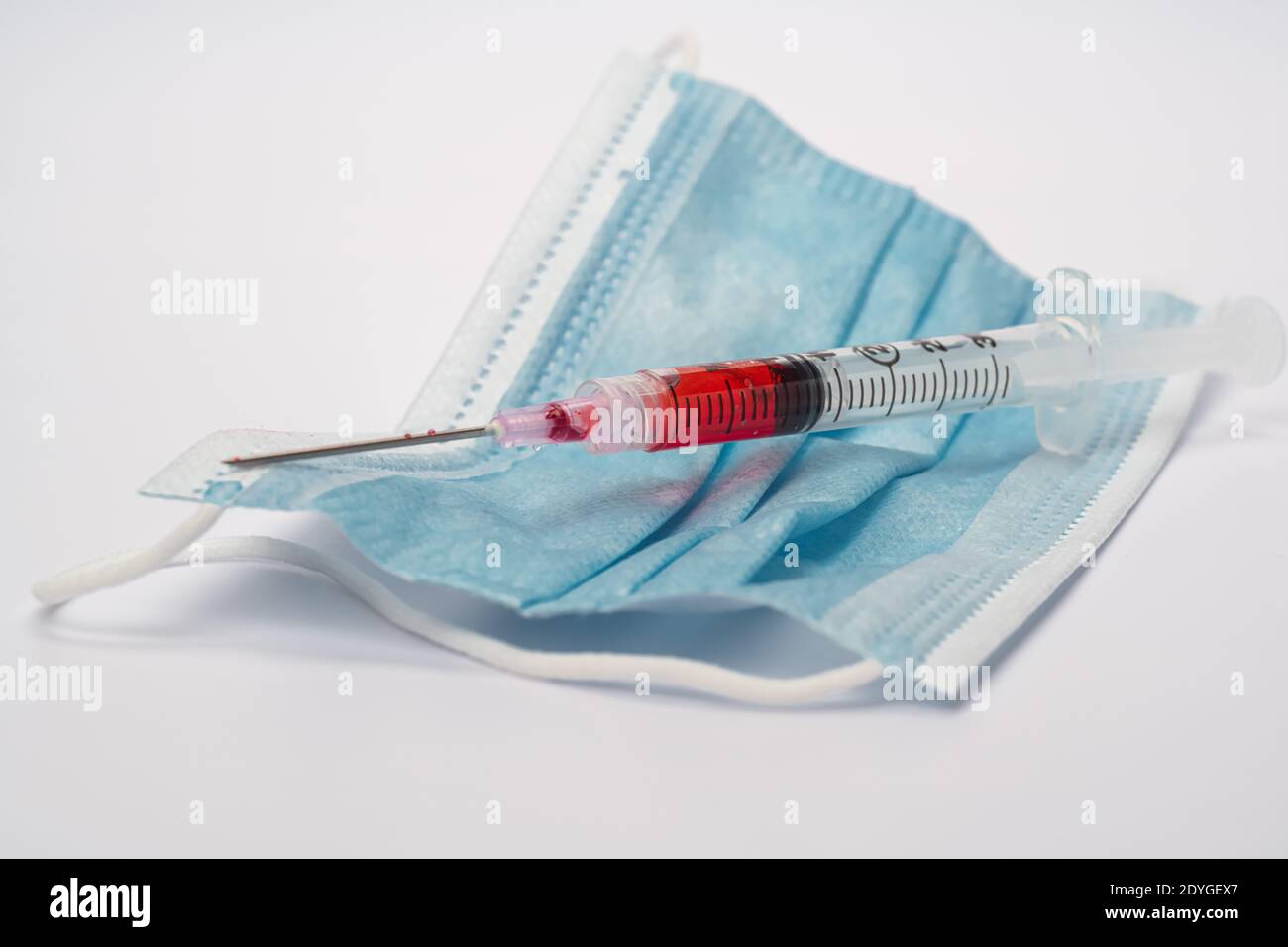 A syringe filled with red liquid, like blood, on a surgical mask ...