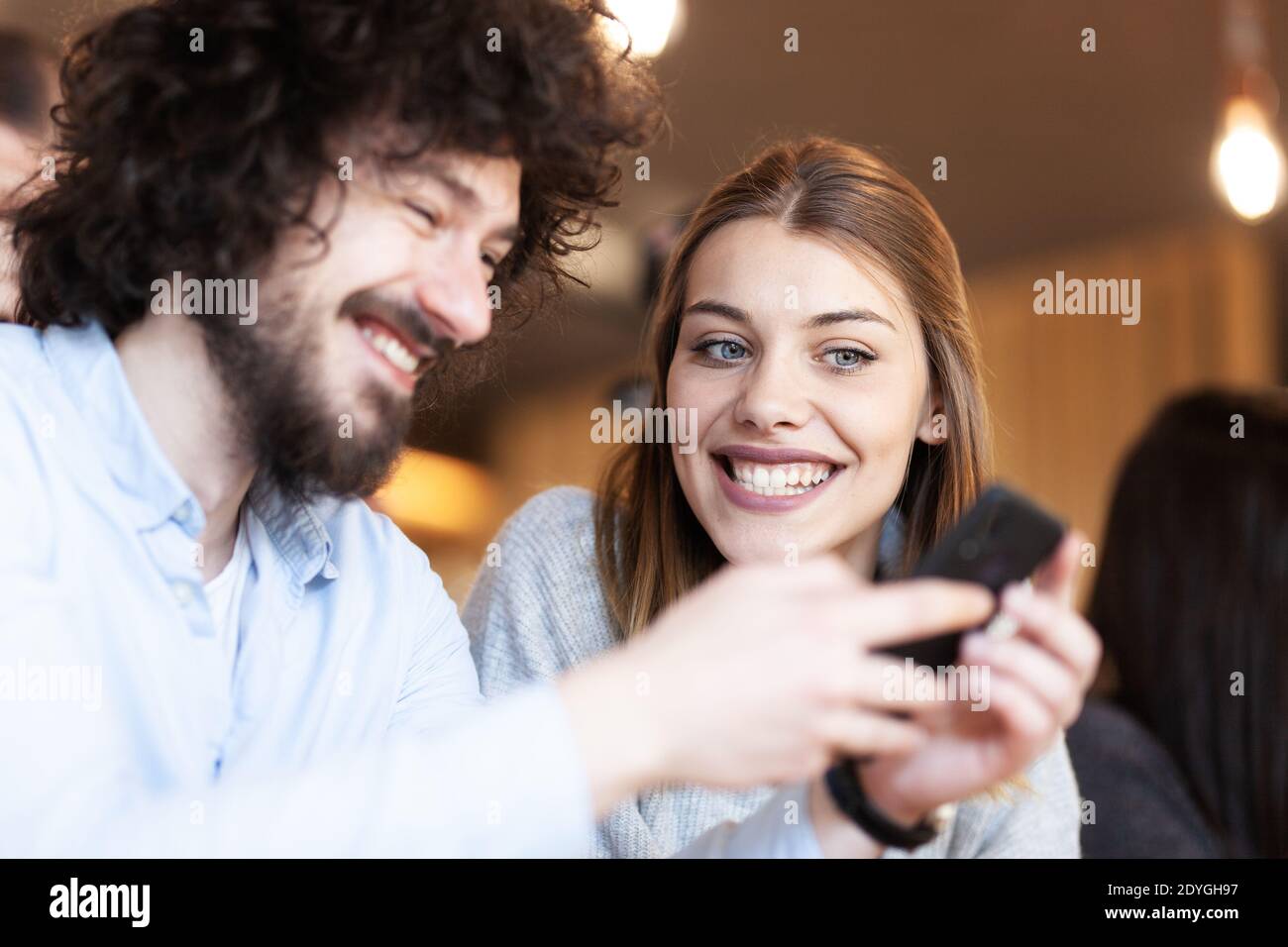 Two friends sitting at a cafe bar looking at phone. Positive and happy ...
