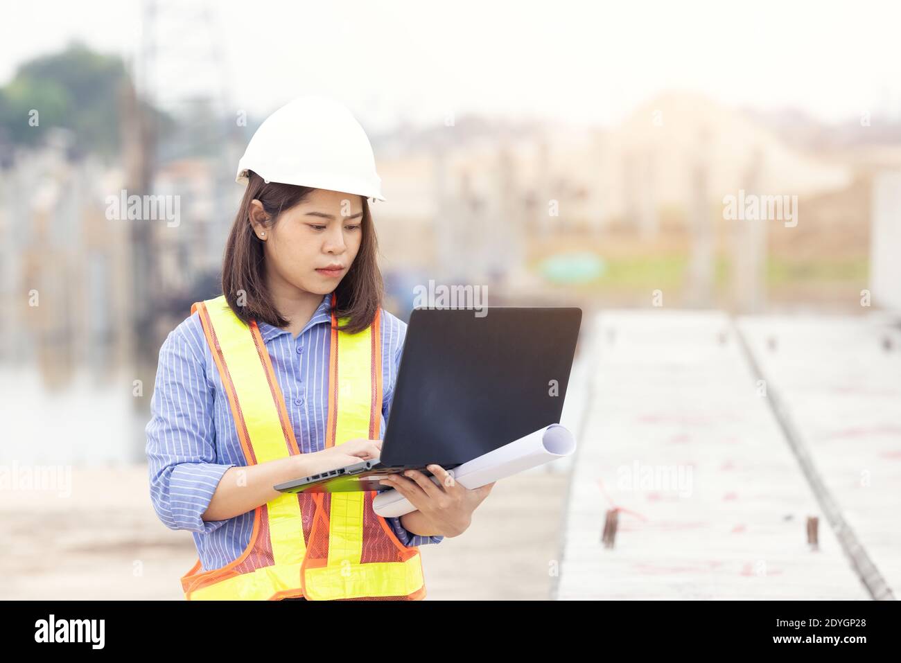 Beautiful Asian female engineer in white safety hard hat using laptop ...