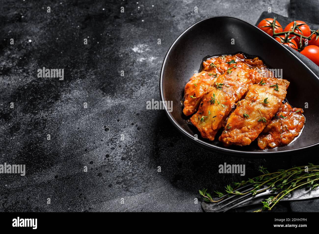 Baked halibut fish with tomato sauce. Black background. Top view. Copy ...