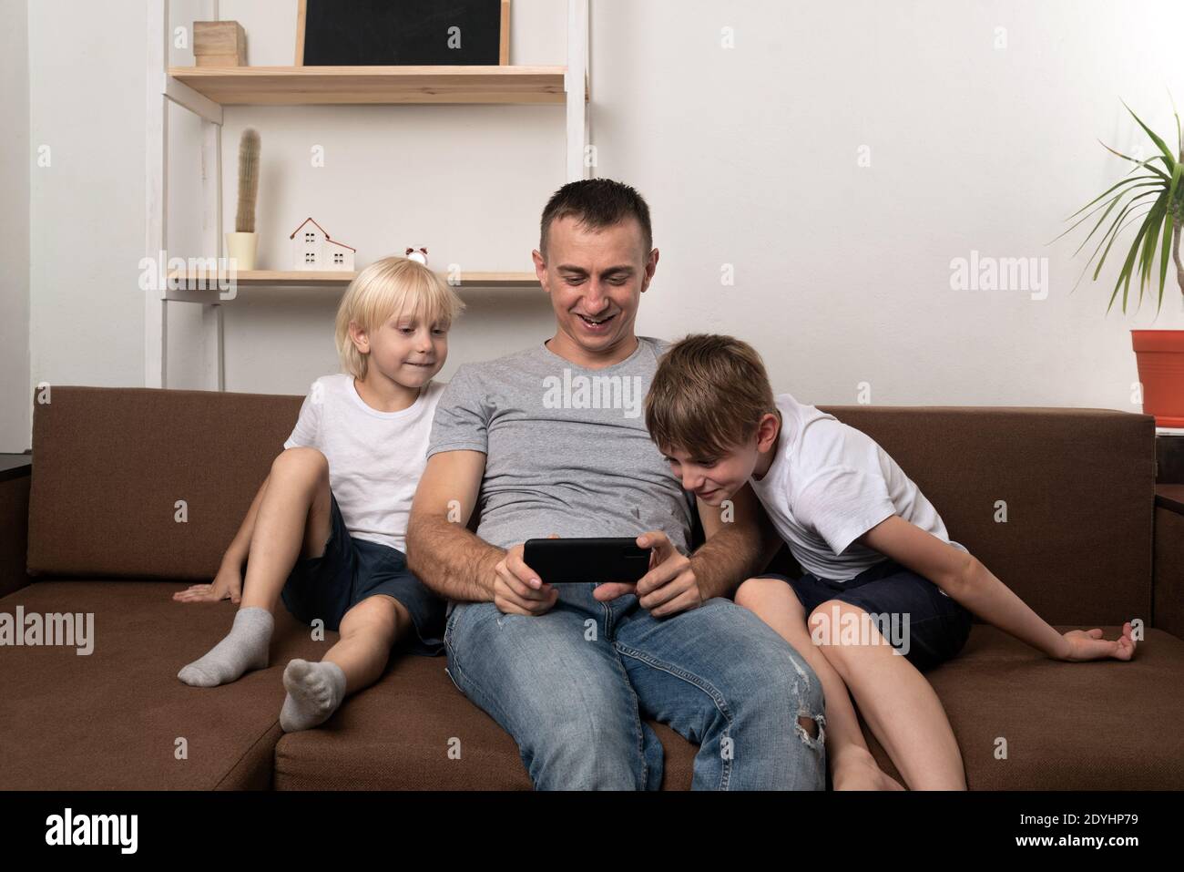 Dad And Two Sons Are Sitting On Couch And Looking At Photo On Phone 2044