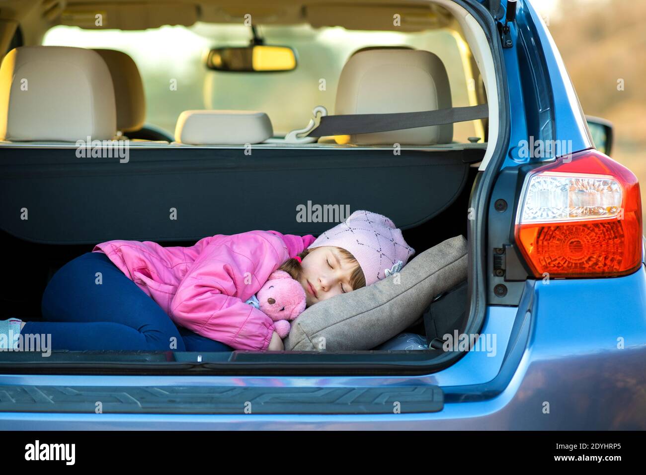 Pretty happy child girl sleeping with a pink toy teddy bear in a car ...