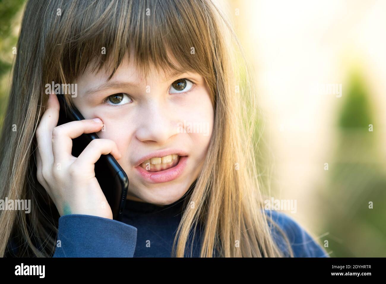 Portrait of angry child girl with long hair talking on cell phone ...