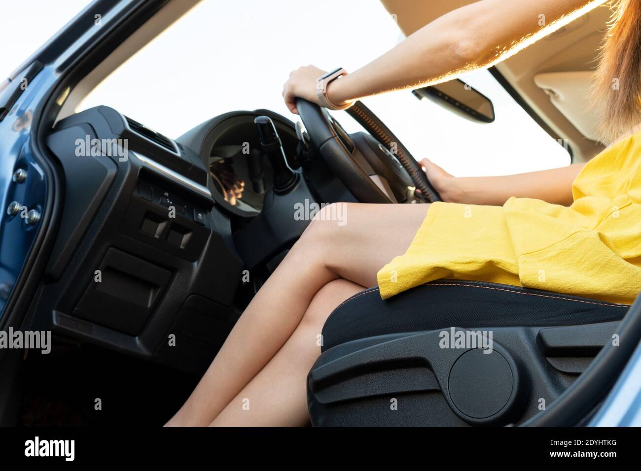 Young woman driver legs in yellow summer dress behind steering wheel ...