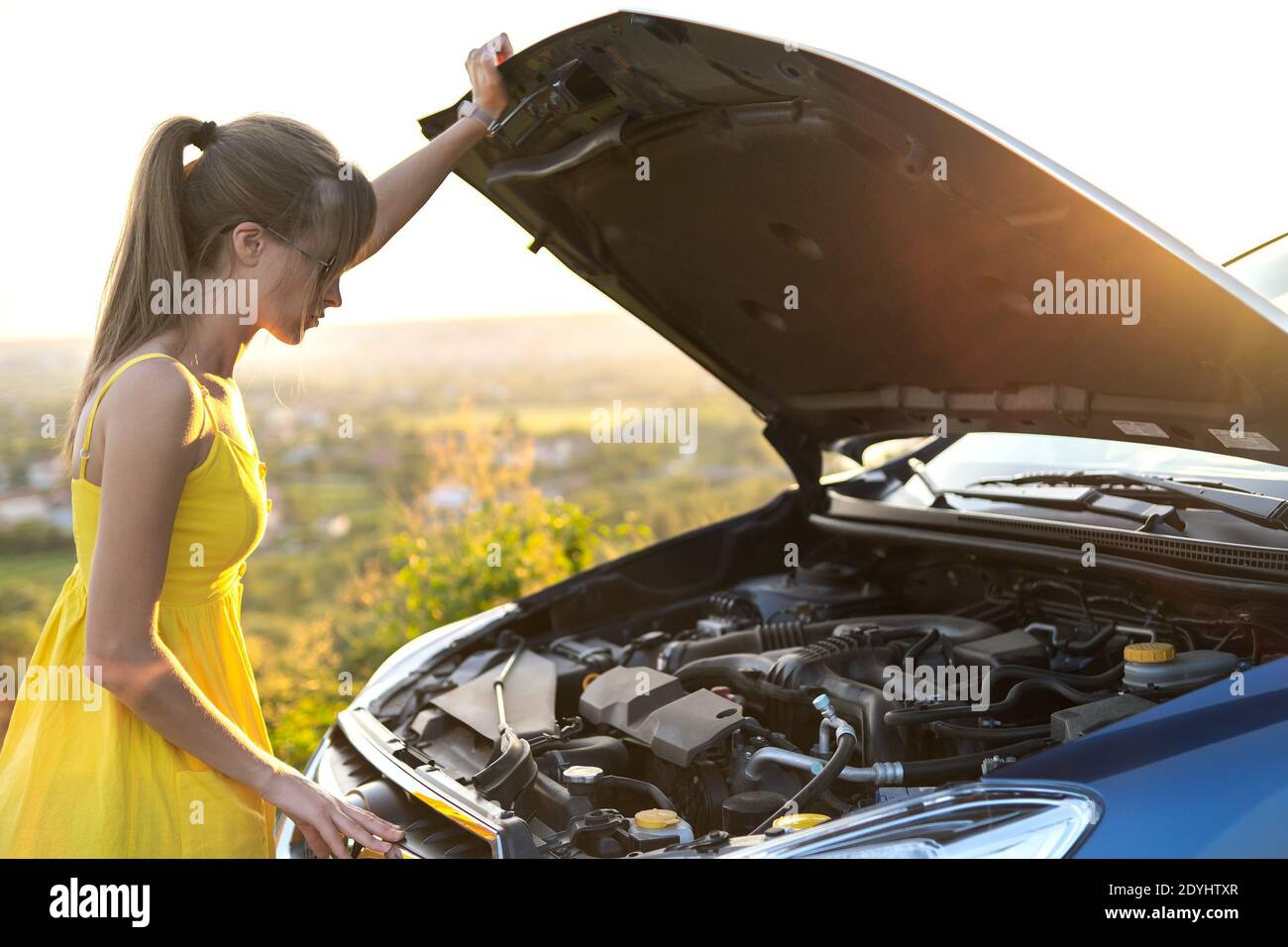Young woman driver standing near her car with popped hood having engine ...
