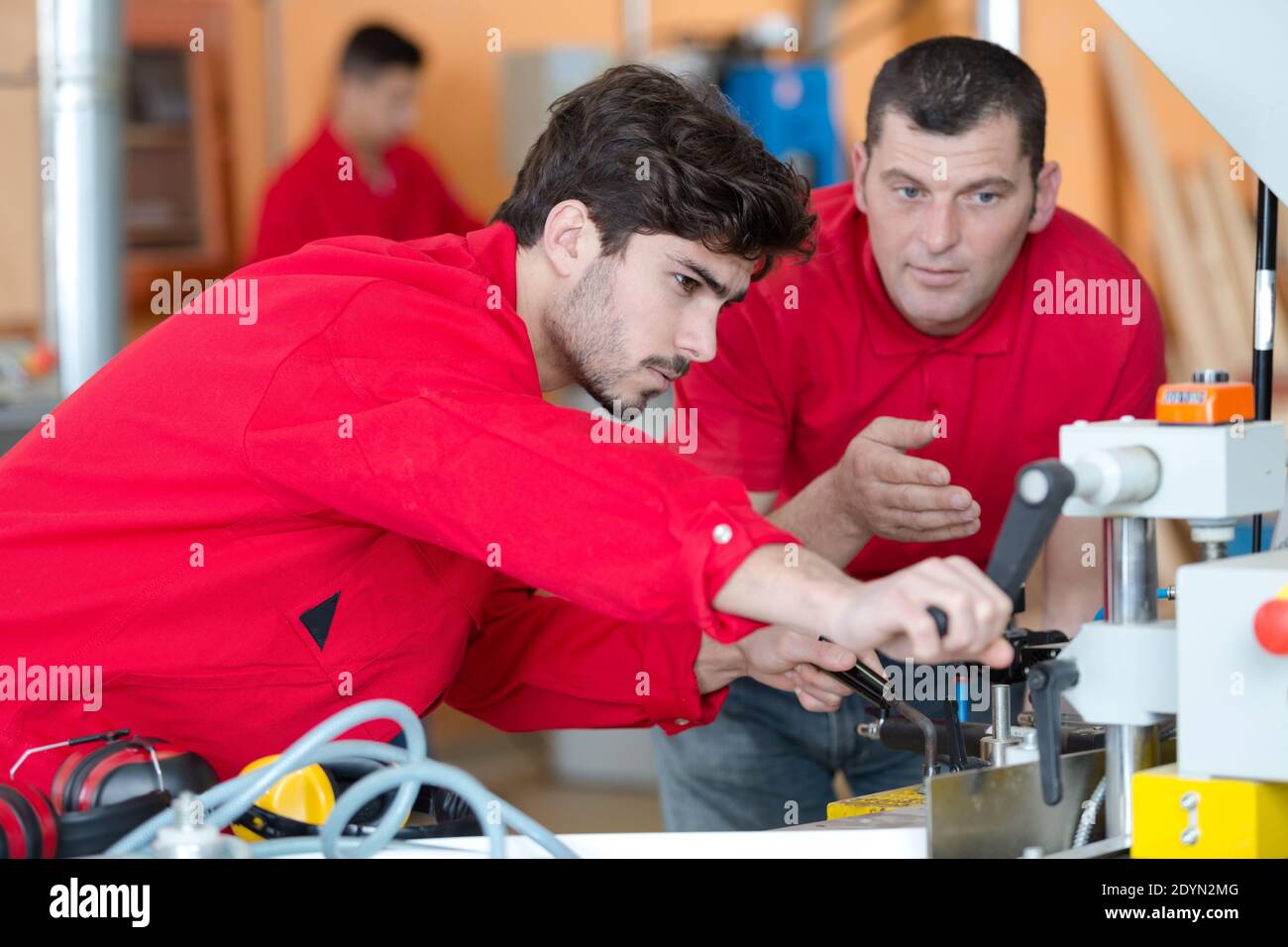 worker and apprentice standing in front of huge industrial machine ...