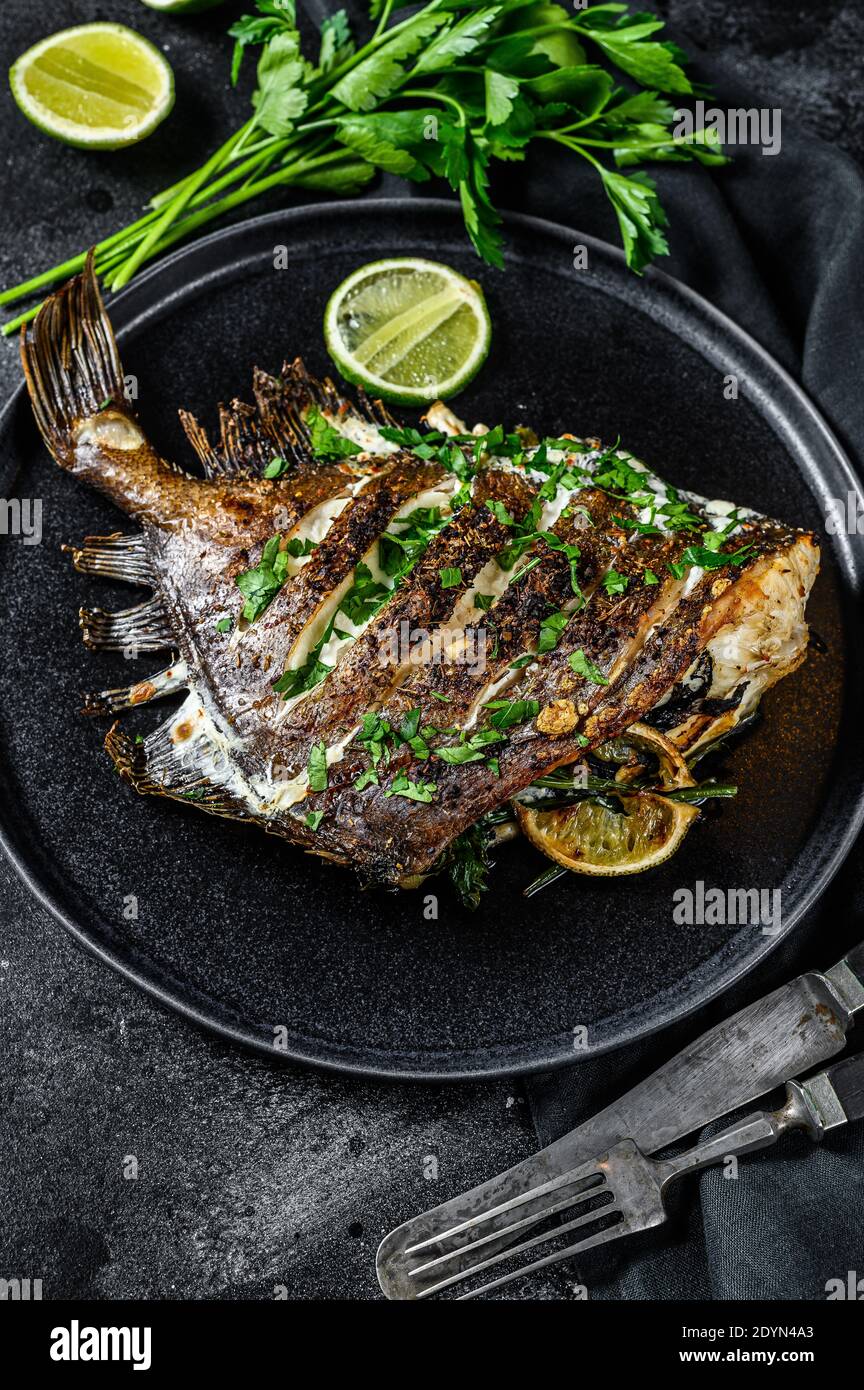 Grilled John Dory fish with lime and parsley in a pan. Black background ...
