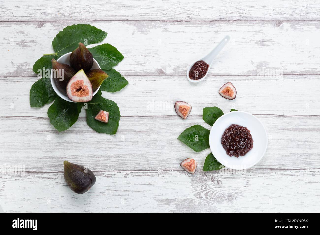 Fig jam with figs, fig leaves and white spoon with jam on White wood ...