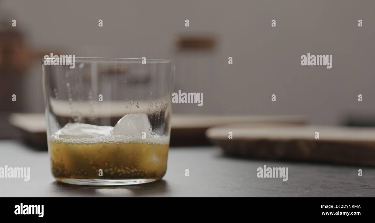 ice into lulo fruit pulp in tumbler glass on concrete countertop, wide ...