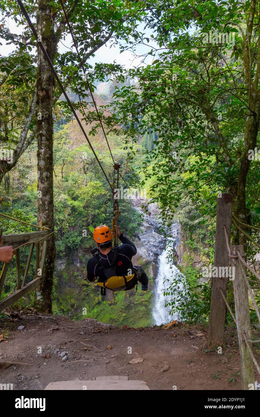 A young man riding on a zip line rope in an extreme adventure jungle in ...