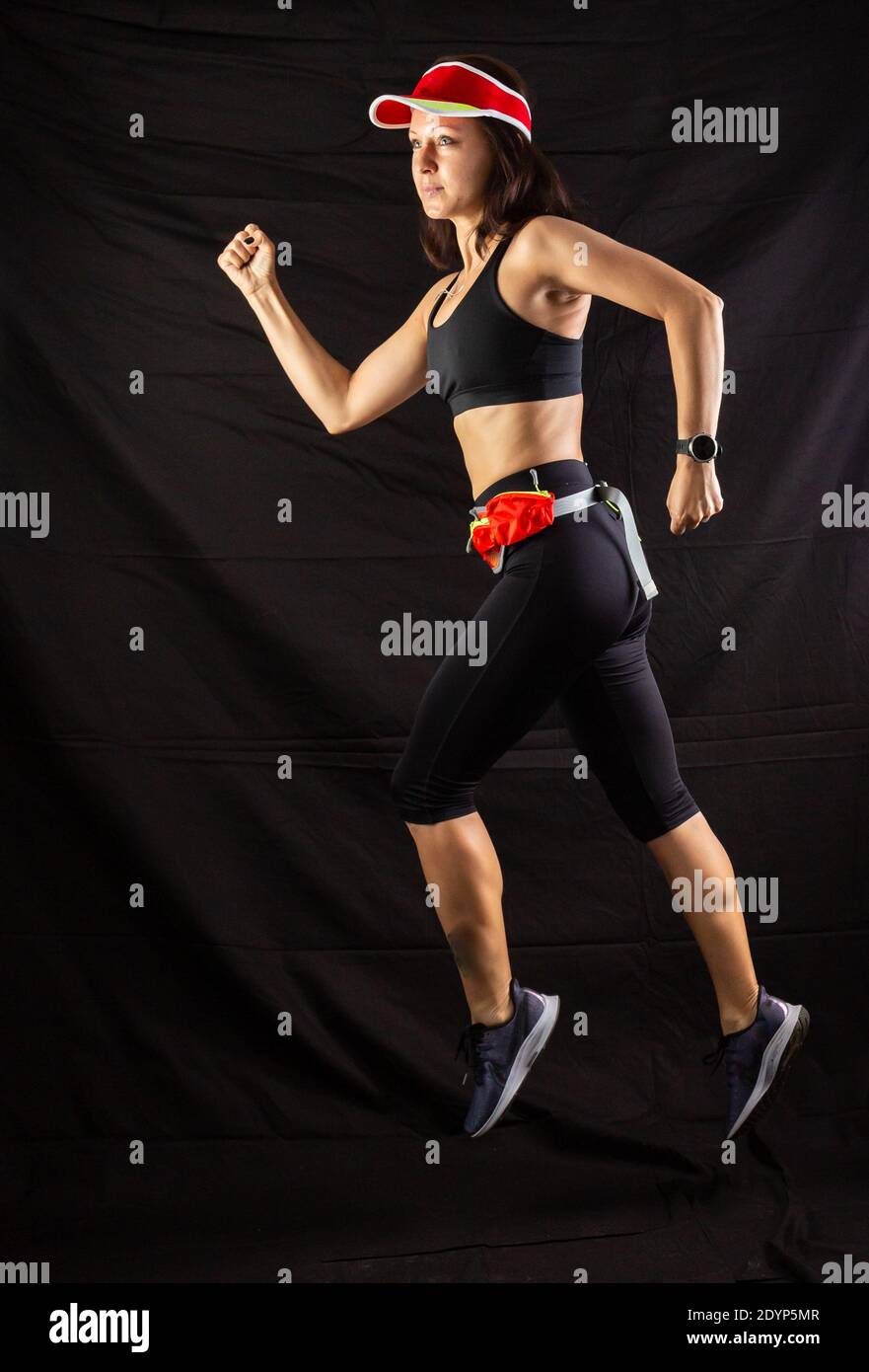 girl in red jogging uniform runs in the studio on a black background ...