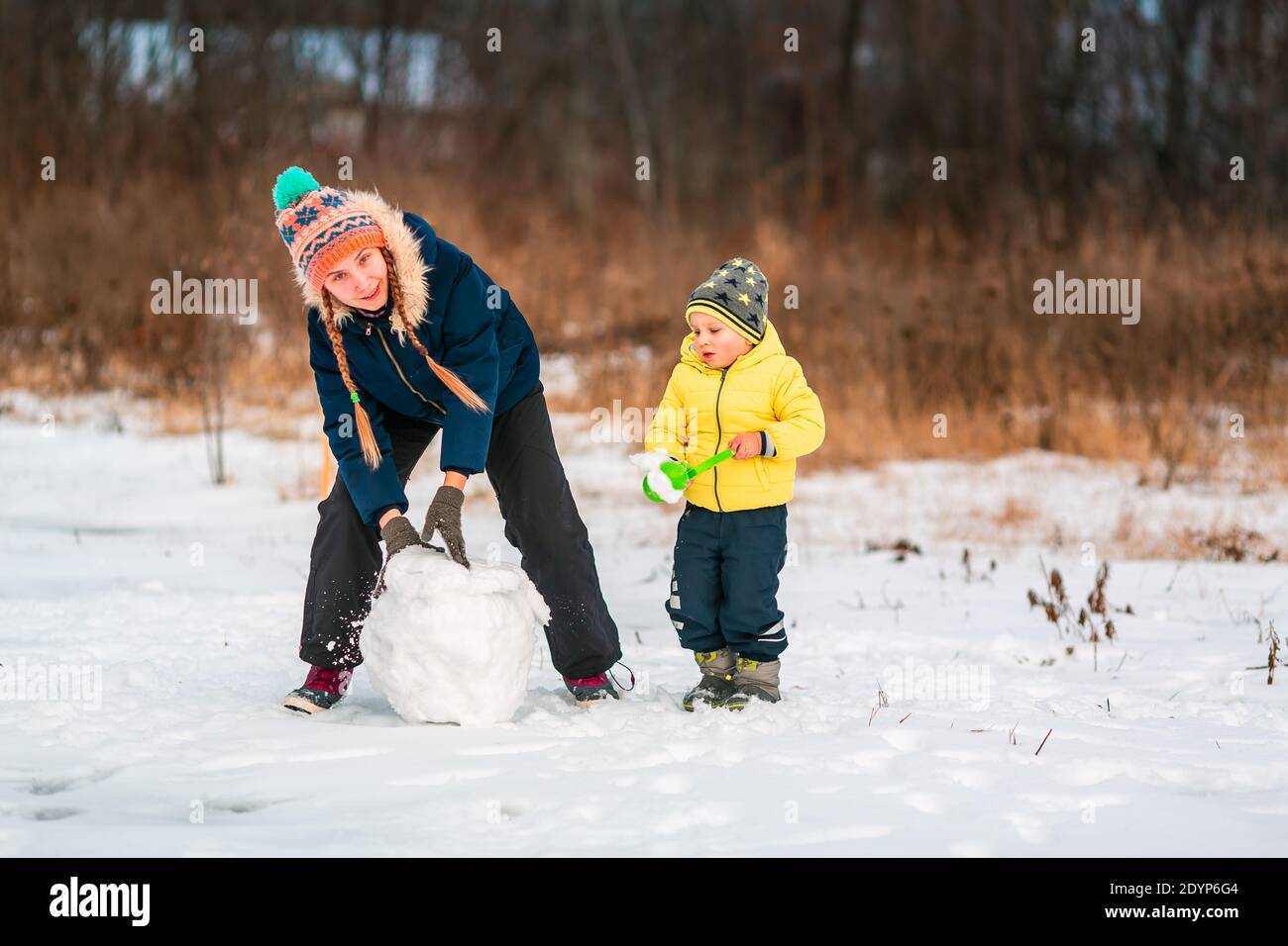 Happy kids making a big snowball to make snowman outdoor in winter ...