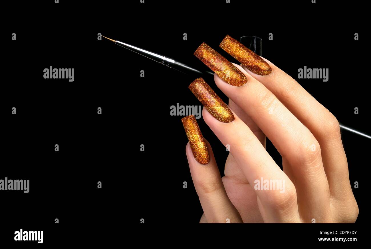 Hand with a beautiful gold manicure and a brush on a black background ...