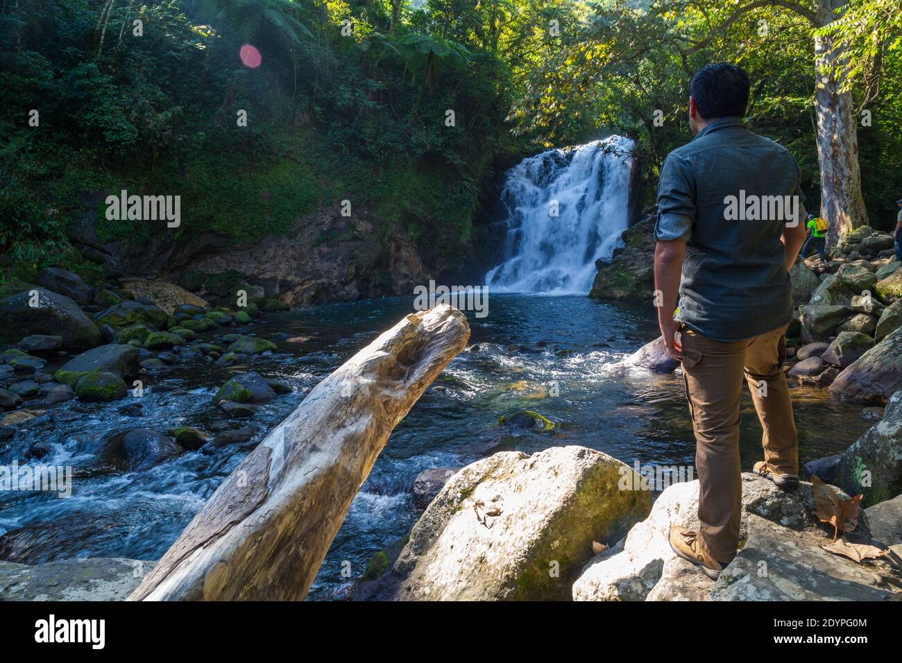 A back view of a young man standing on rocks looking at a flowing ...
