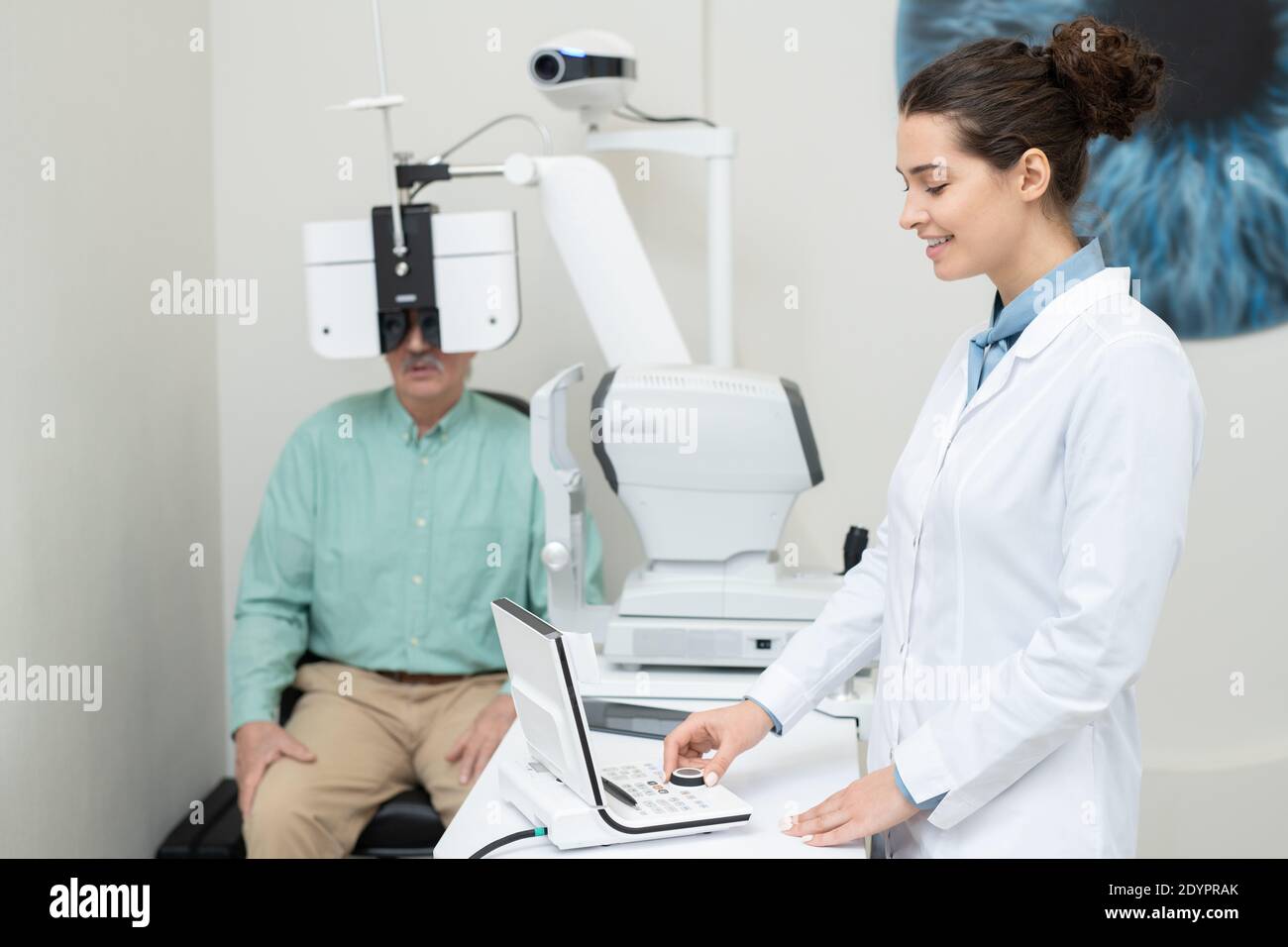 Happy young female ophthalmologist in whitecoat standing in front of ...
