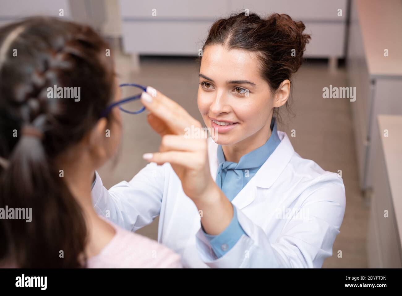 Happy young female ophthalmologist in whitecoat putting pair of new ...