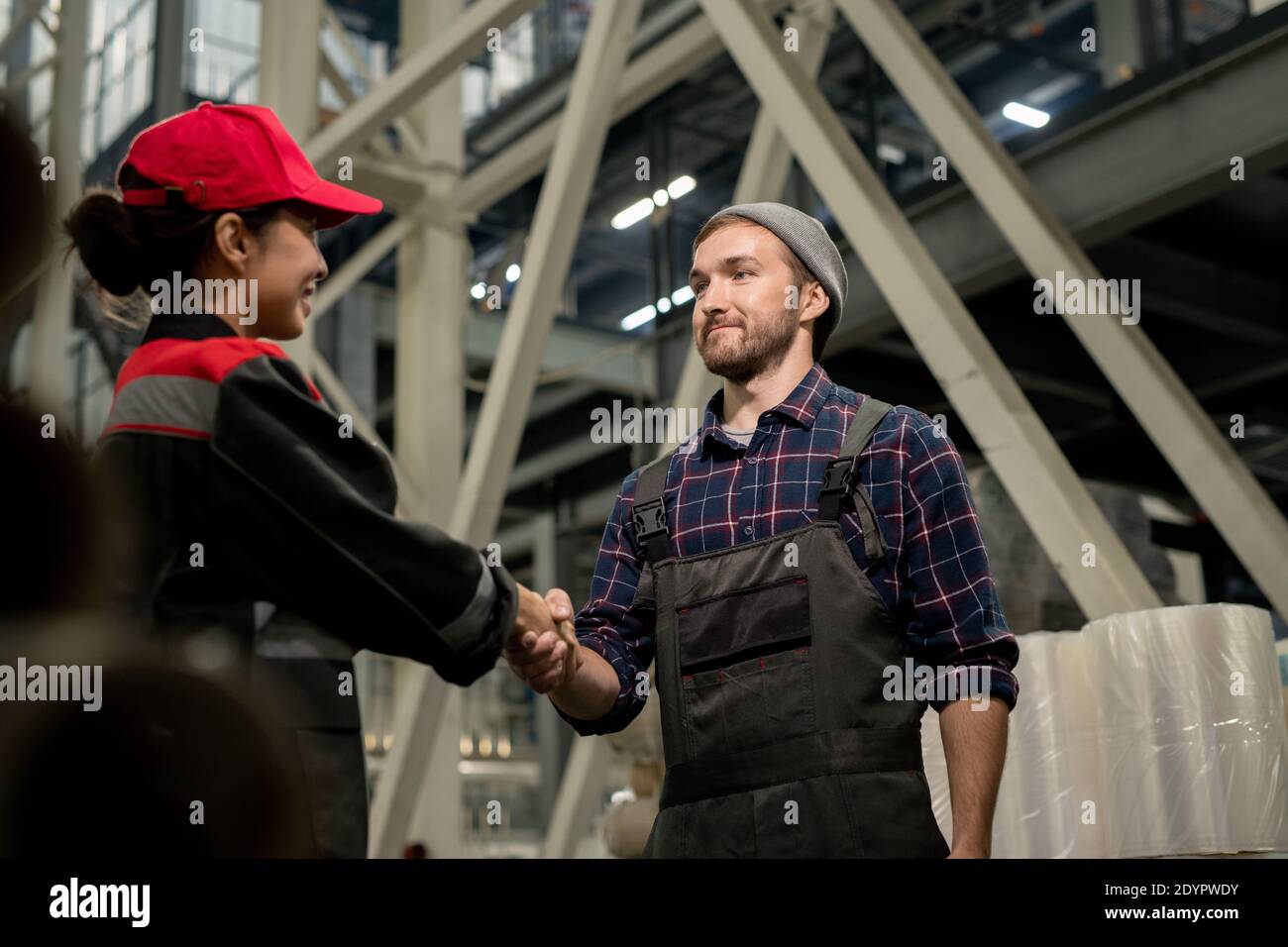 Young successful engineer in overalls and checkered shirt shaking hand ...