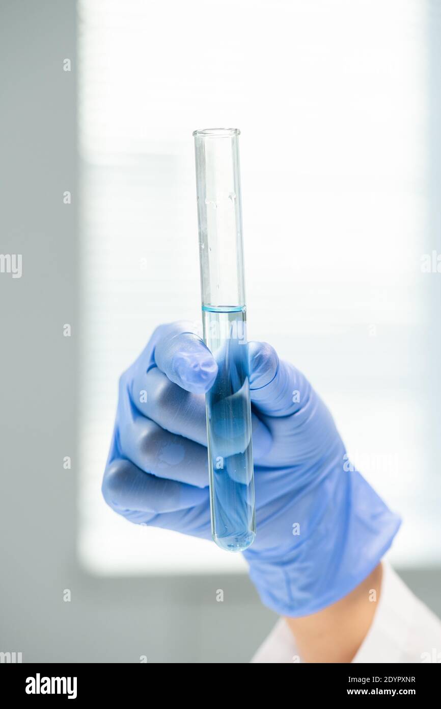 Gloved hand of contemporary young researcher holding flask with pure ...